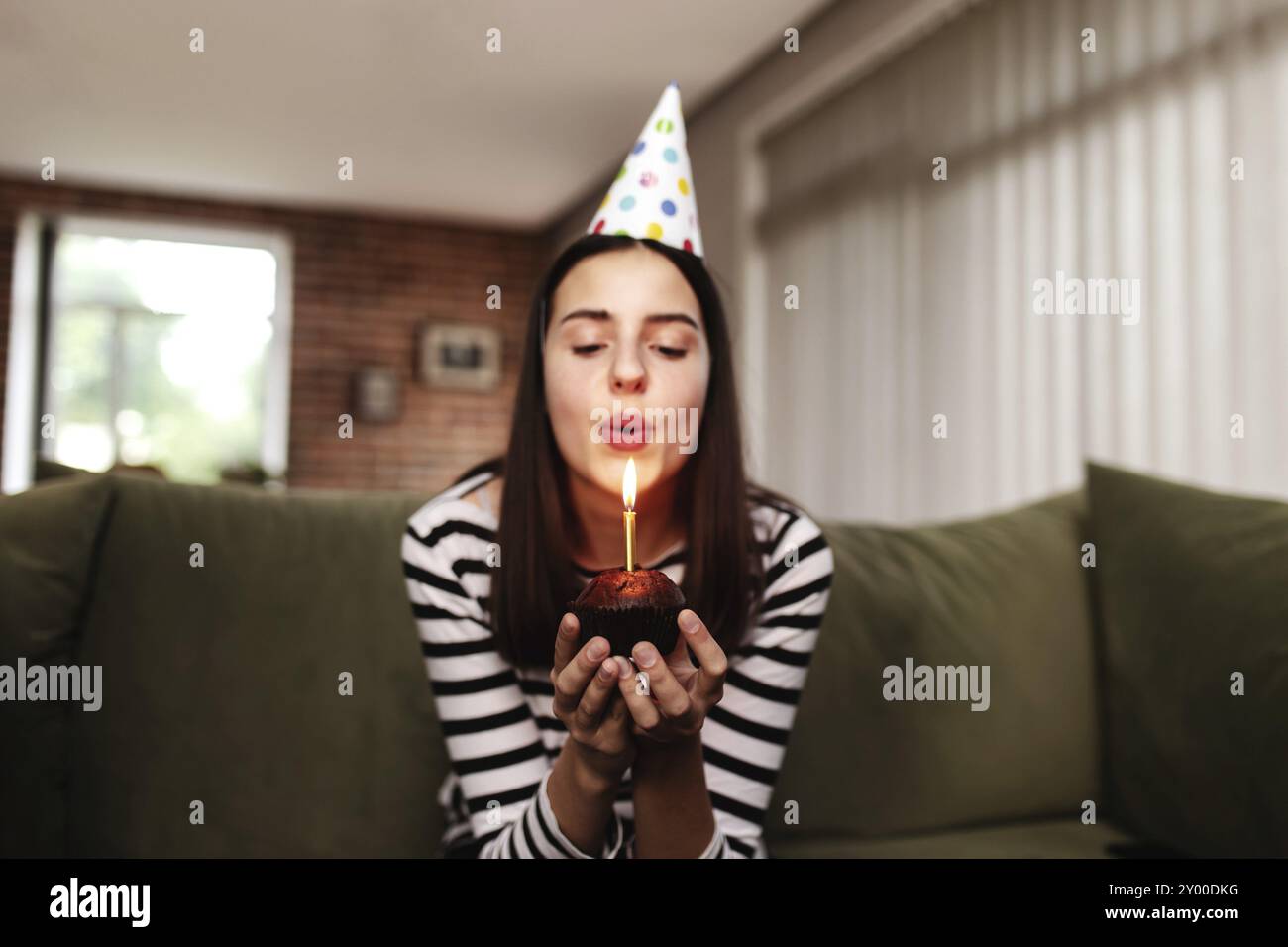 Birthday girl brunette in cardboard hat sits on the couch or sofa and ...