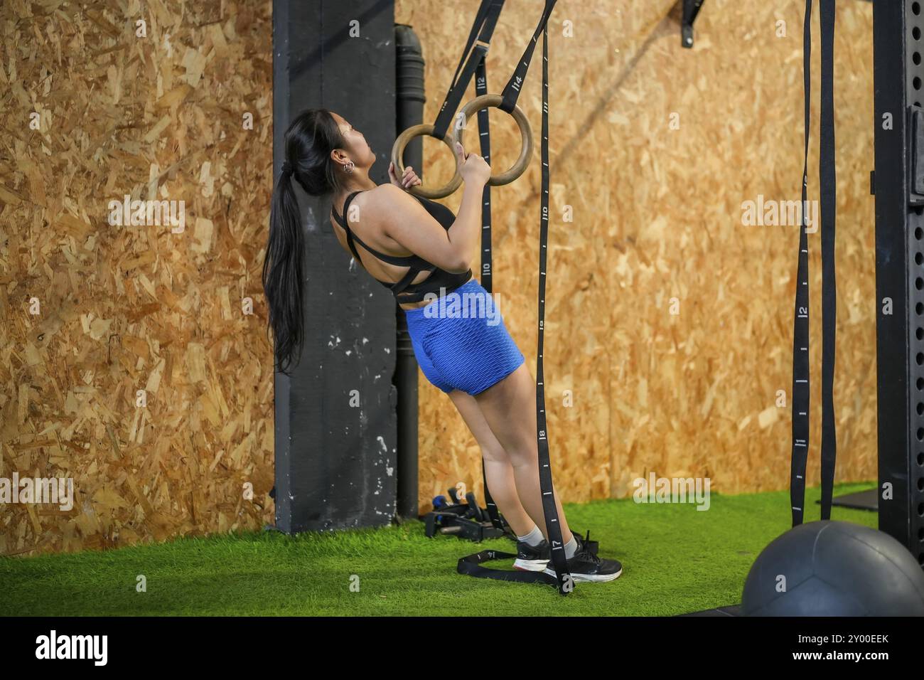 Full length side view of an asian woman exercising using gym rings to do pull-ups Stock Photo ...