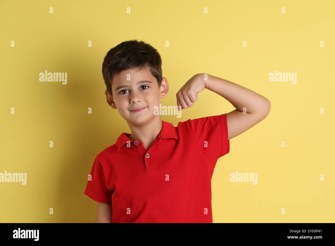 Cute little boy showing his bicep on yellow background Stock Photo - Alamy