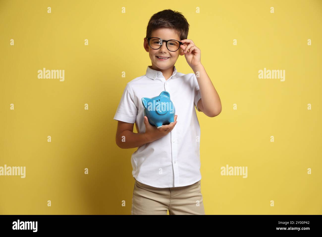 Pocket money. Cute boy with piggy bank on yellow background Stock Photo ...