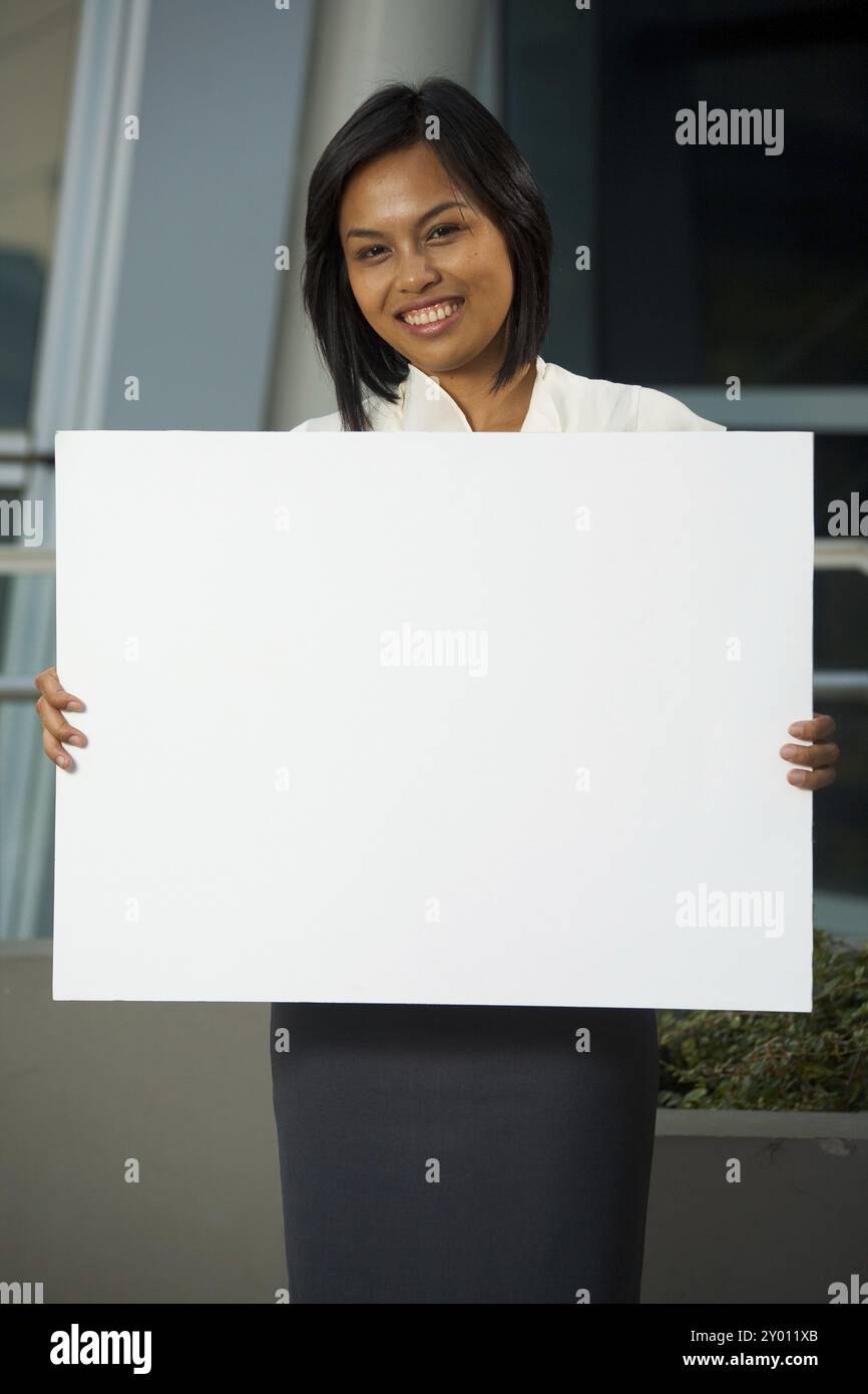 A beautiful smiling corporate woman holds a blank sign for custom text ...