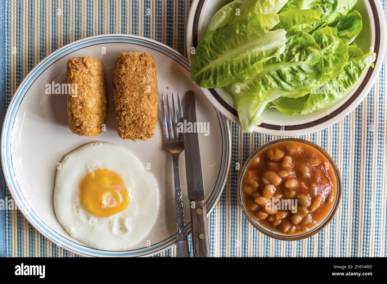 Croquettes, fried egg, fresh vegetables, white kidney beans in tomato ...
