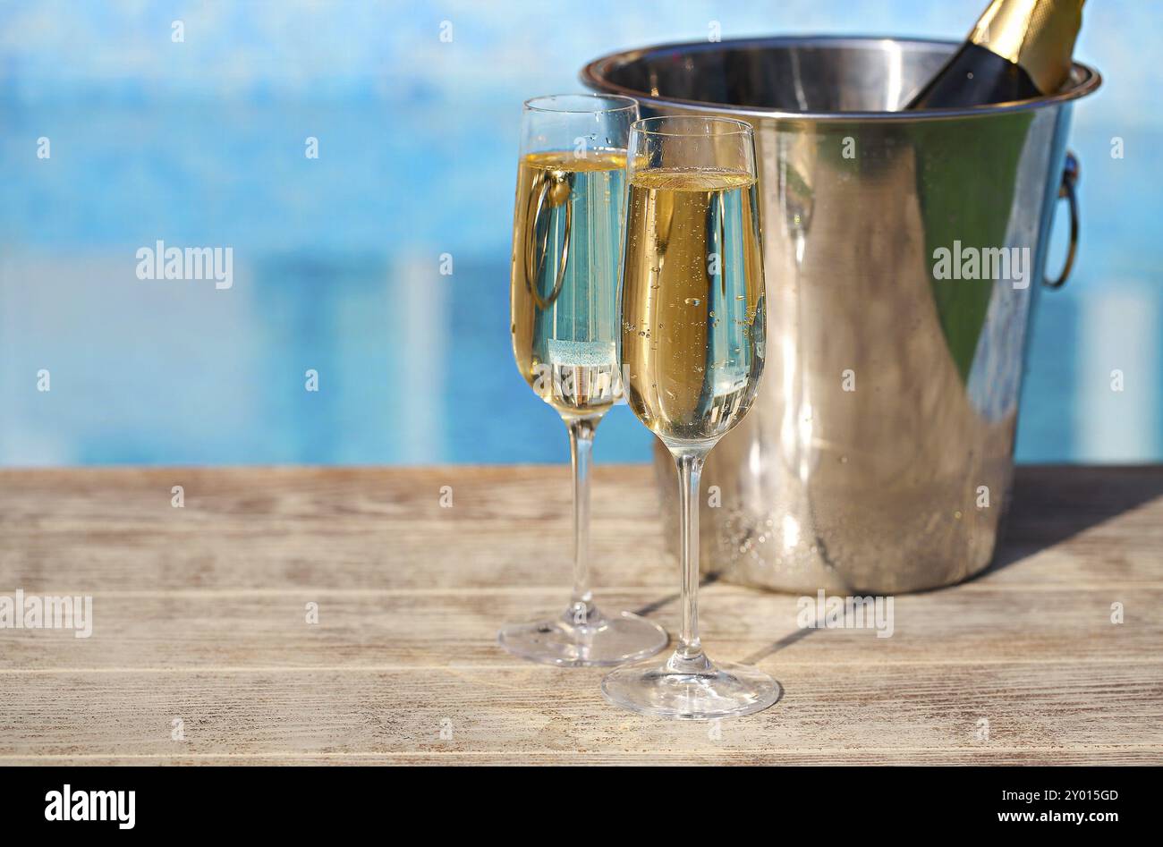Champagne glasses and bottle in ice bucket near swimming pool. Vacation ...