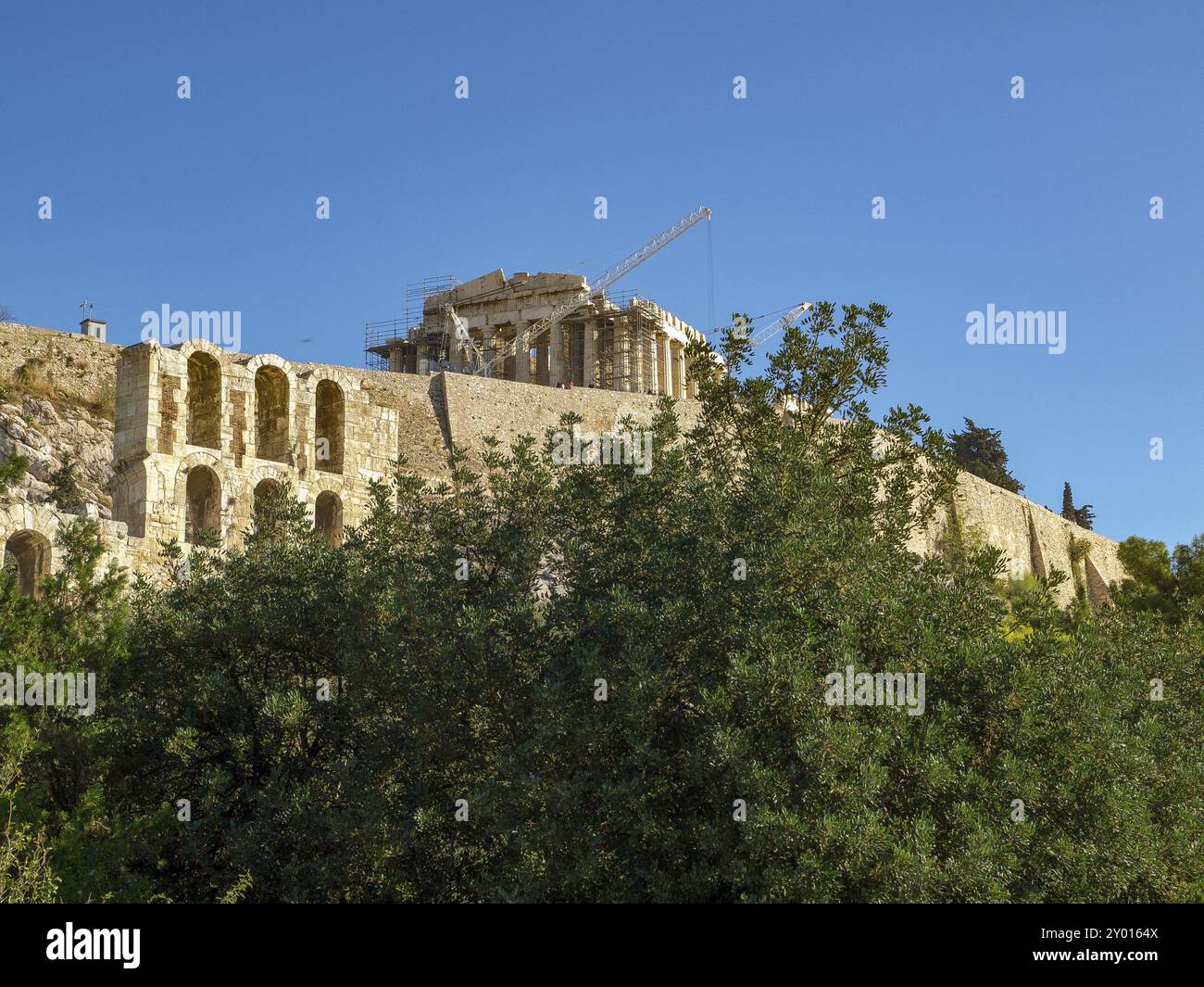 Ancient ruins and buildings tower over lush greenery and trees under a clear blue sky, athens ...