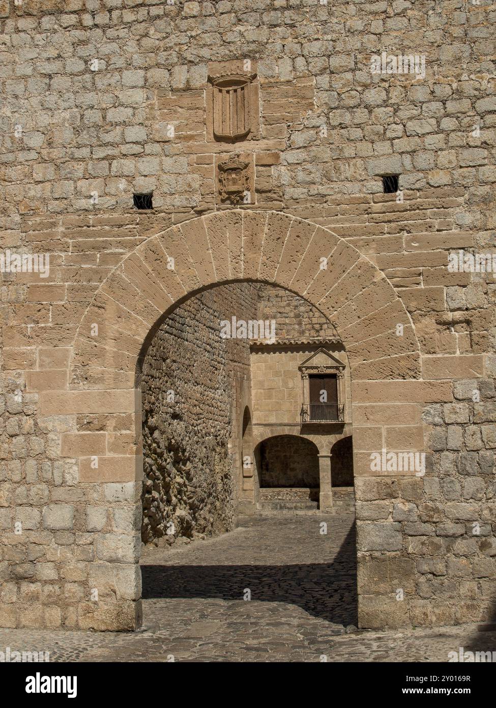 Stone wall with archway leading into a shady courtyard, surrounded by ...