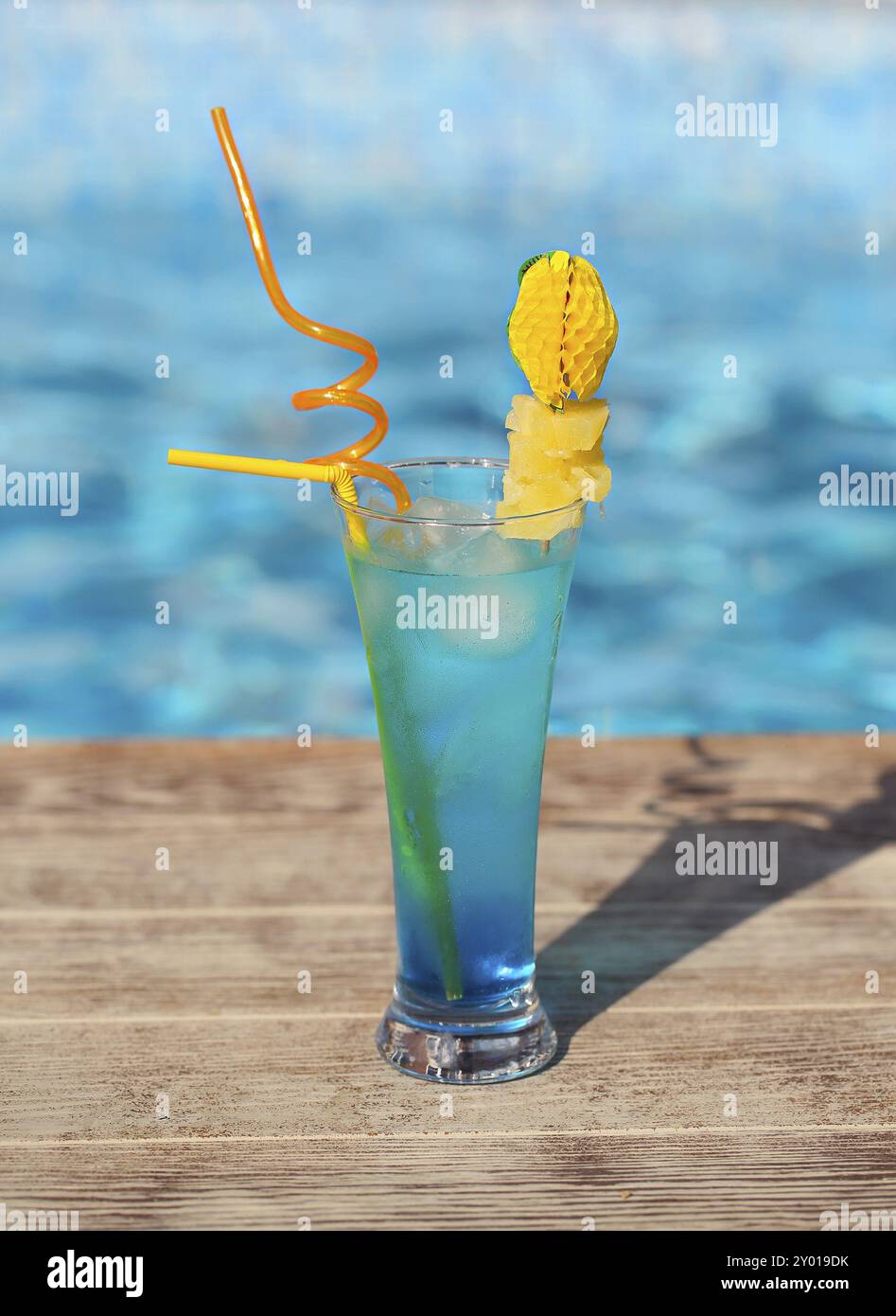 Glass with a bright blue lagoon cocktail on the table by the pool ...