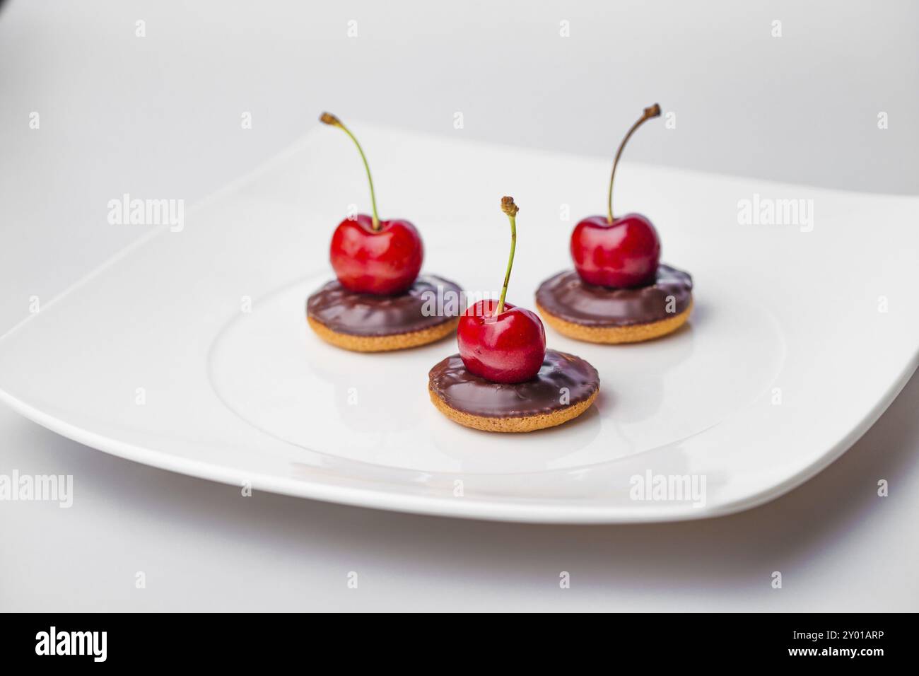Three cherries on three chocolate biscuits Stock Photo - Alamy