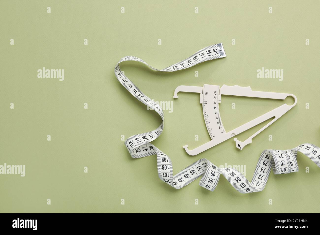 Body fat caliper and measuring tape on light green background, flat lay ...