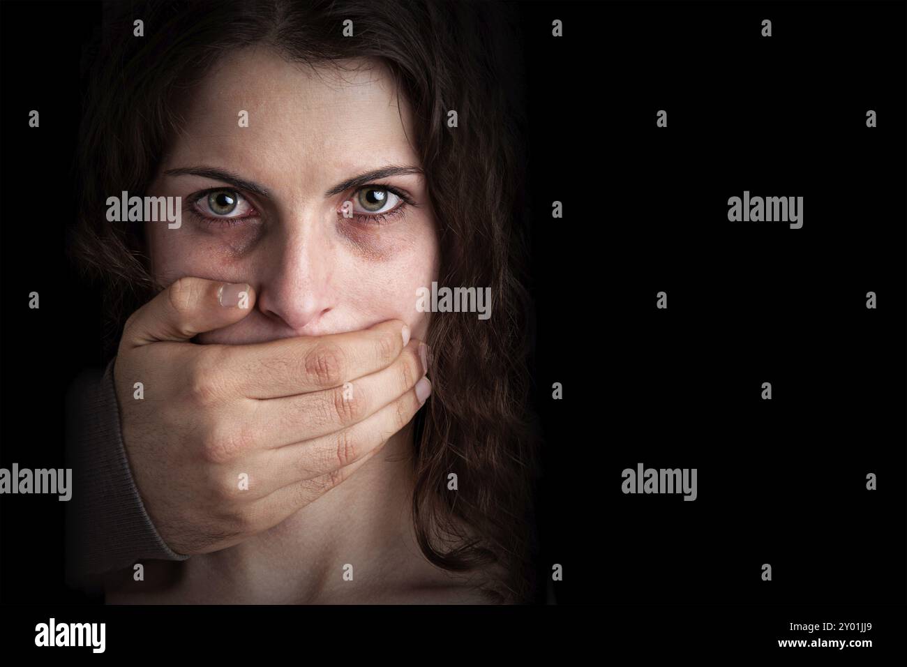 Closeup of a mans hand covering a womans mouth. Concept of domestic violence or kidnapping. Dark ...