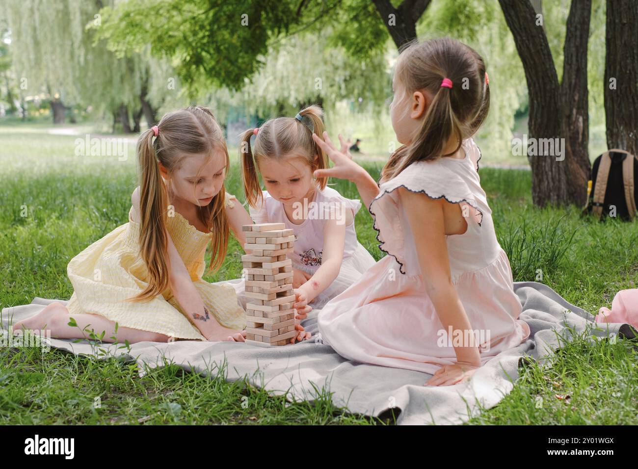 Three girls playing fun game. Children carefully stacking wooden blocks ...