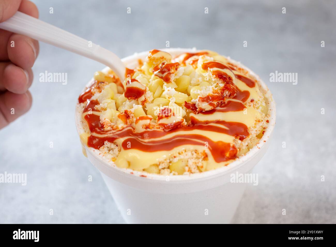 A view of a hand and spoon scooping a bite of esquites Stock Photo - Alamy