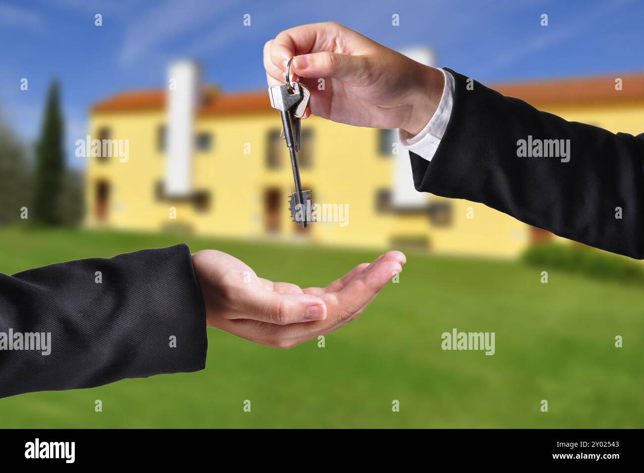 A hand giving a key to another hand. Both persons in suits. House in ...