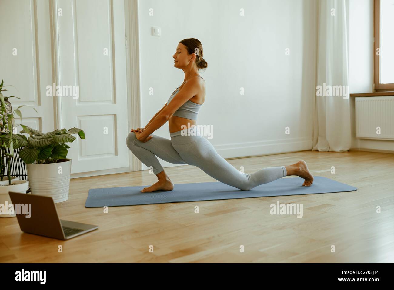 A woman is practicing yoga at her home while wearing comfortable and ...
