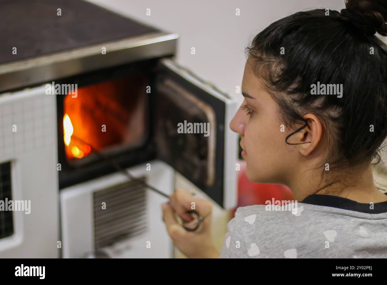 Poor teen girl putting firewood in the stove indoors at home, poverty ...