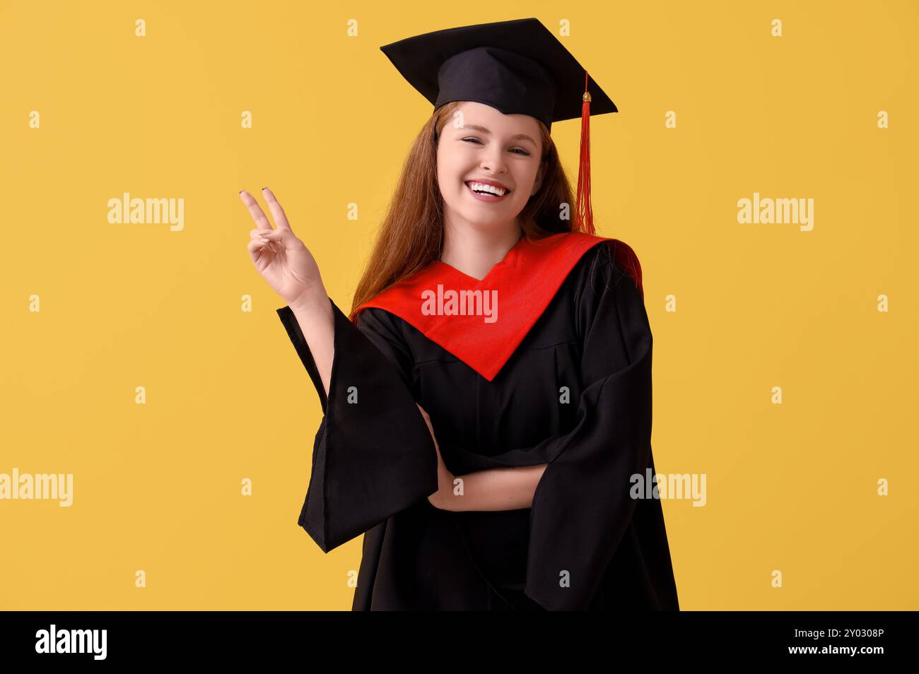 Female graduate student showing victory gesture on yellow background ...