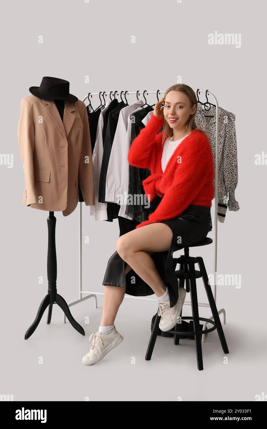 Happy female stylist with clothes on rack sitting against grey ...