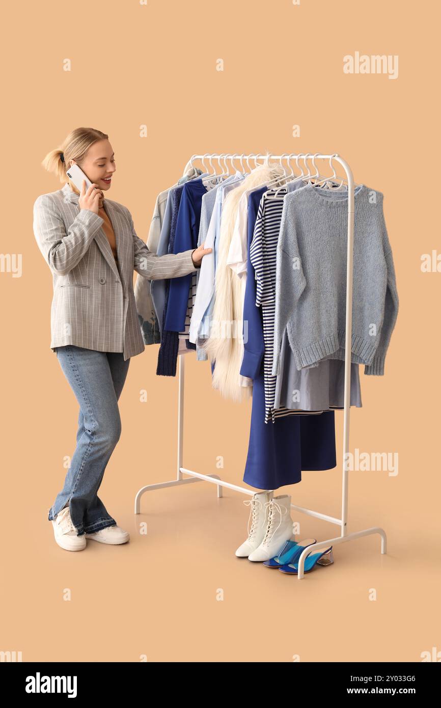 Female stylist with clothes on rack talking by mobile phone against ...