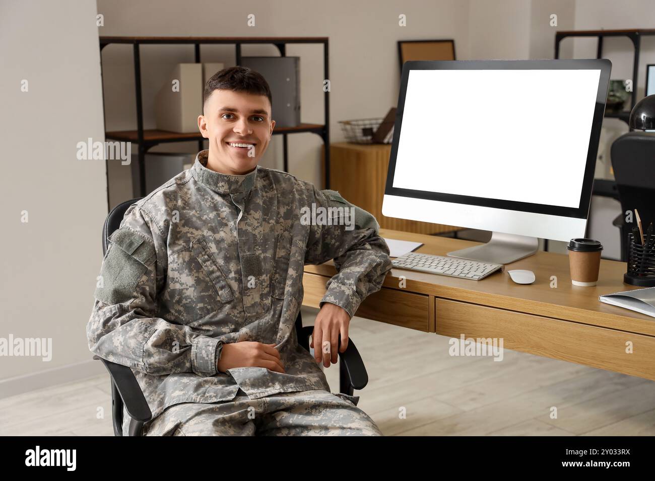 Young male soldier sitting at table with blank computer screen in ...