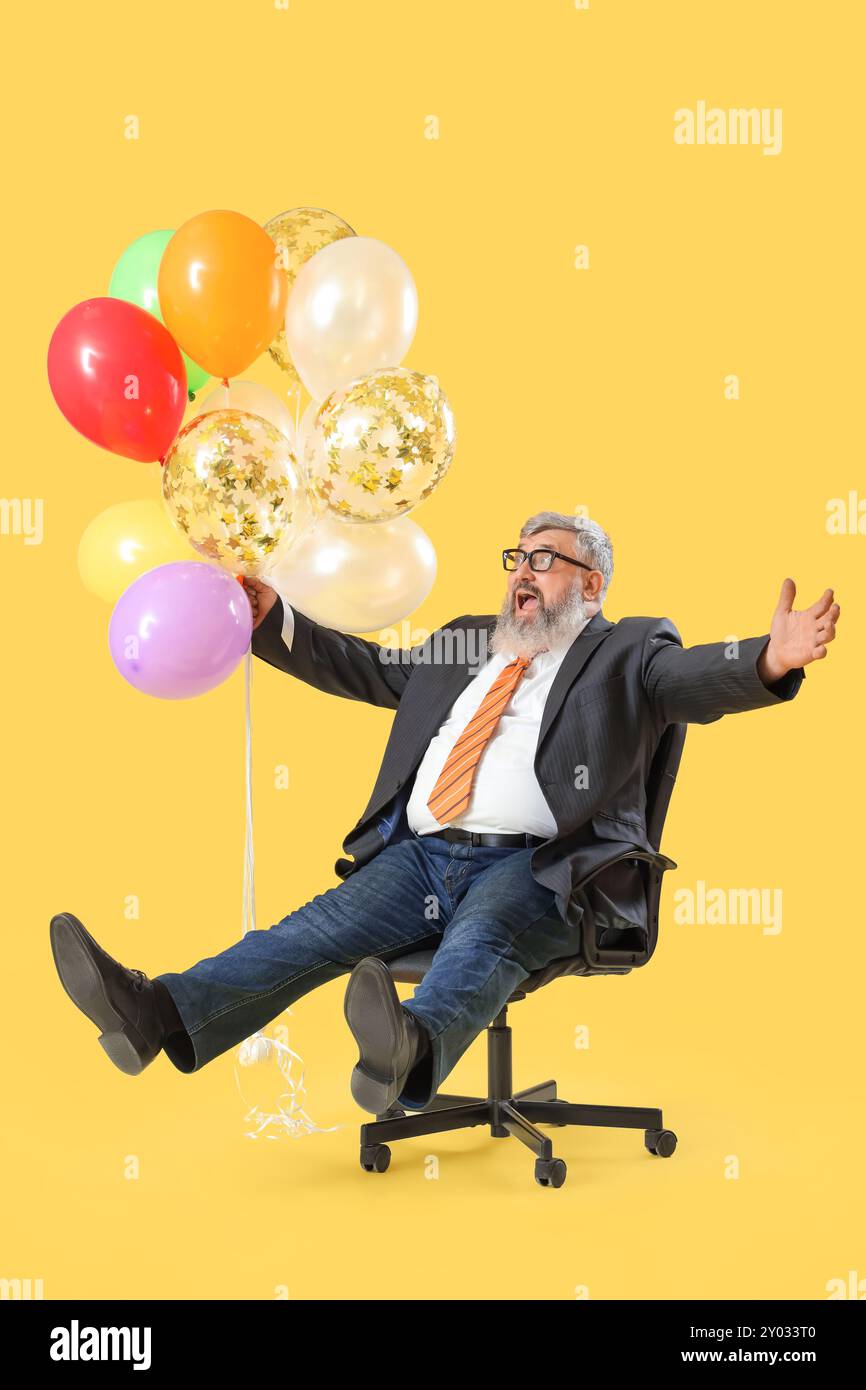 Senior businessman with bunch of colorful balloons sitting on chair ...