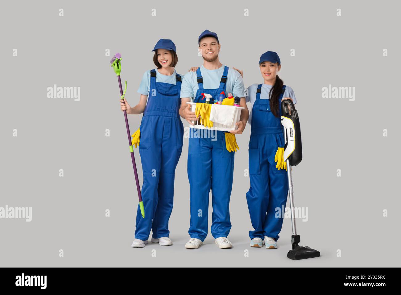 Young janitors with cleaning supplies on grey background Stock Photo ...