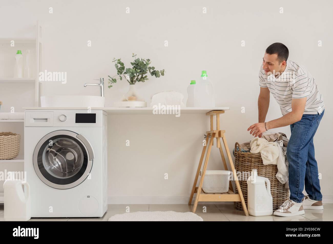 Young man taking dirty clothes from basket in laundry room Stock Photo ...