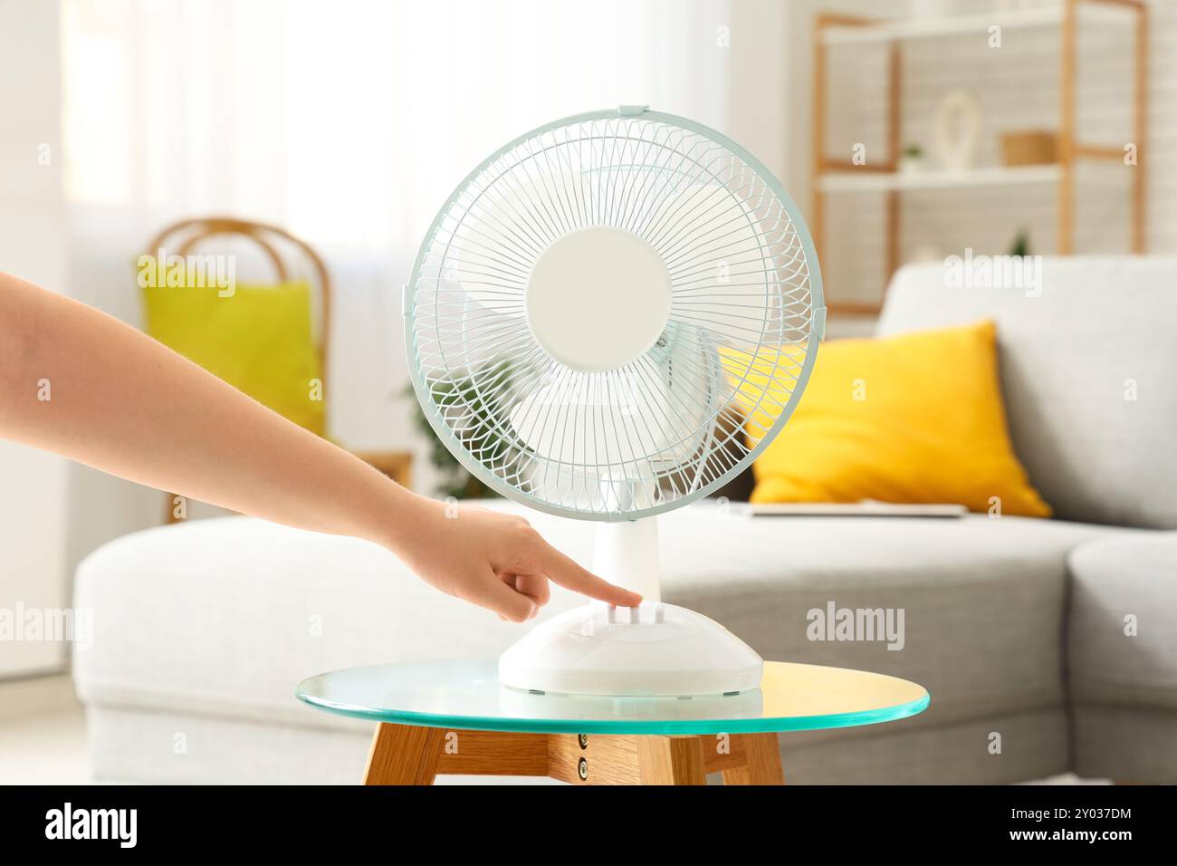 Woman turning on modern electric fan on coffee table at home Stock ...
