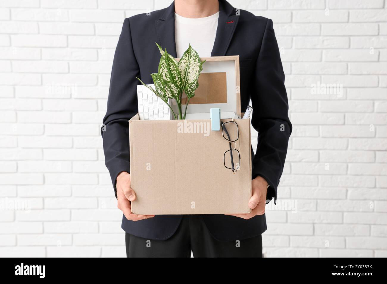 Fired young businessman holding box with personal stuff on white brick ...