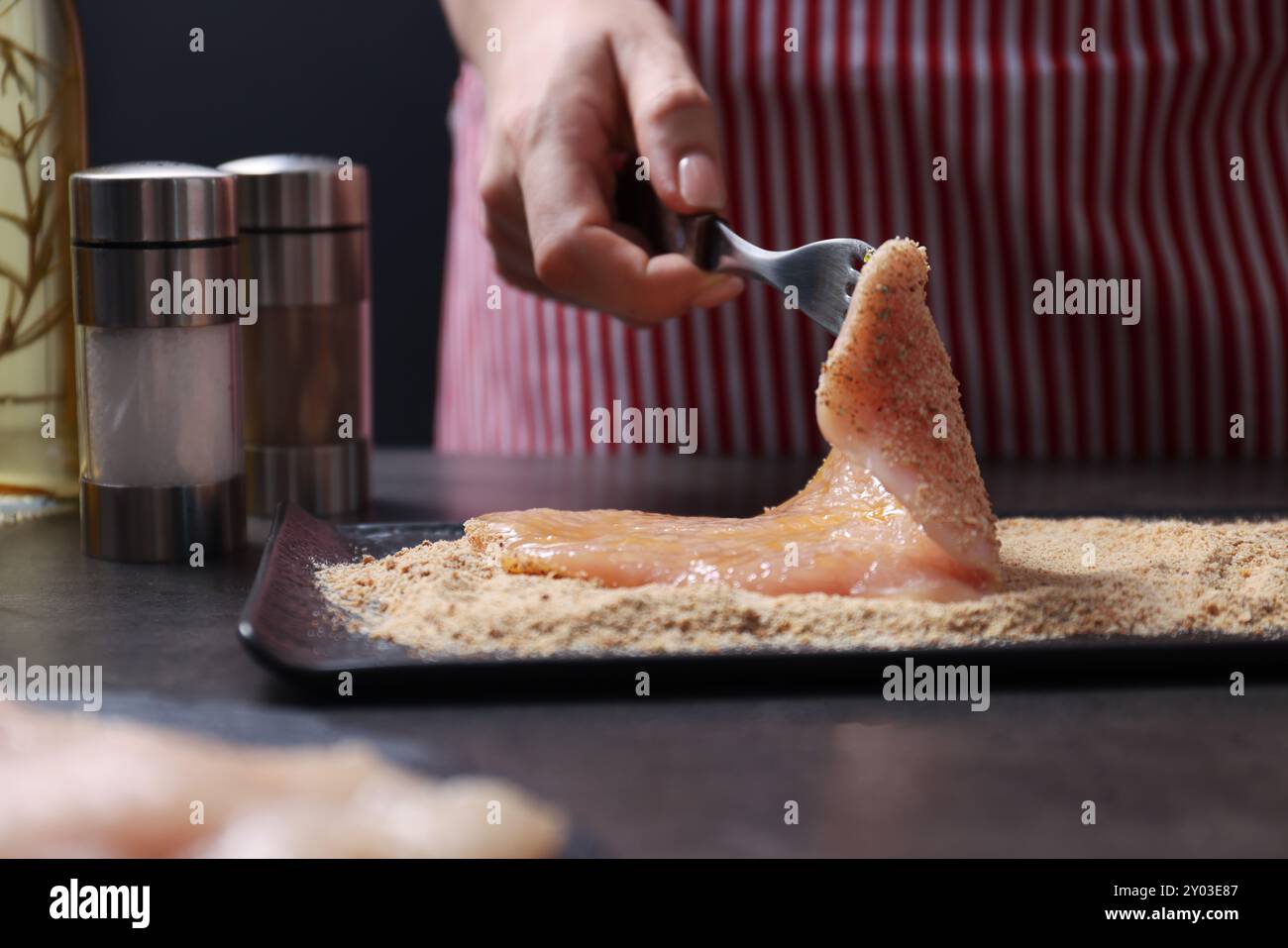 Making schnitzel. Woman coating slice of meat with bread crumbs at dark ...