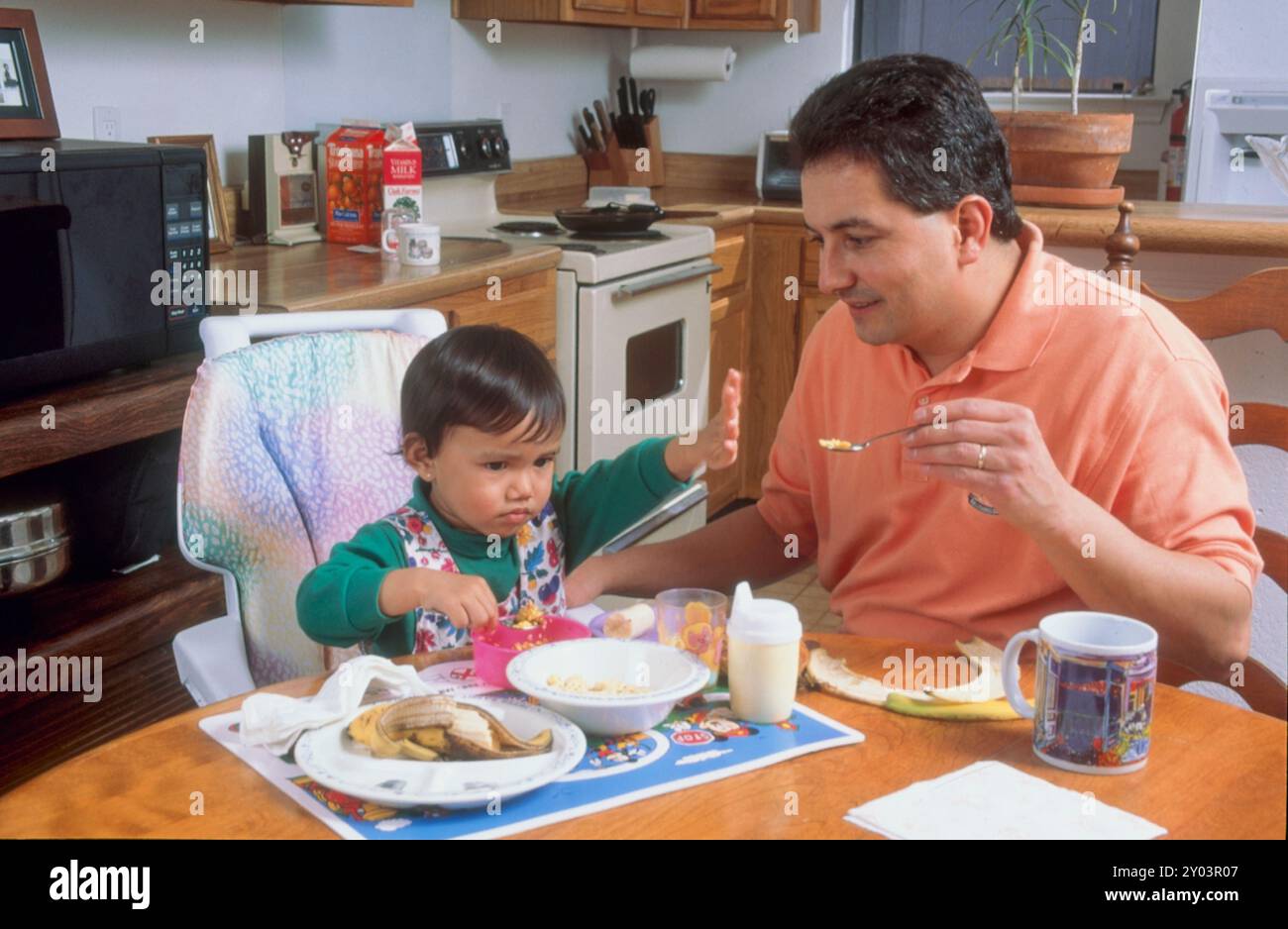 Hispanic father sitting at the kitchen table feeding his 16-month-old ...