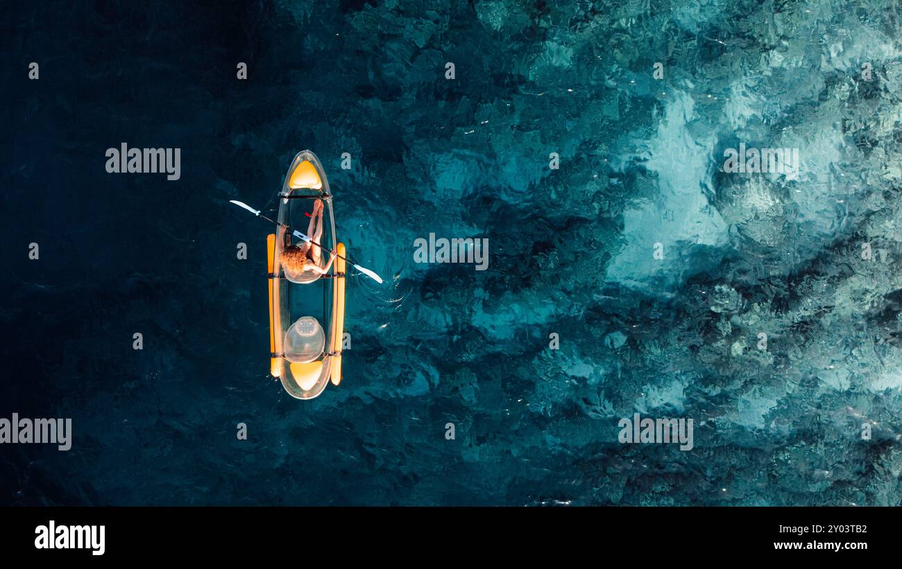 Woman kayaking in blue ocean on transparent kayak. Drone view with copy ...