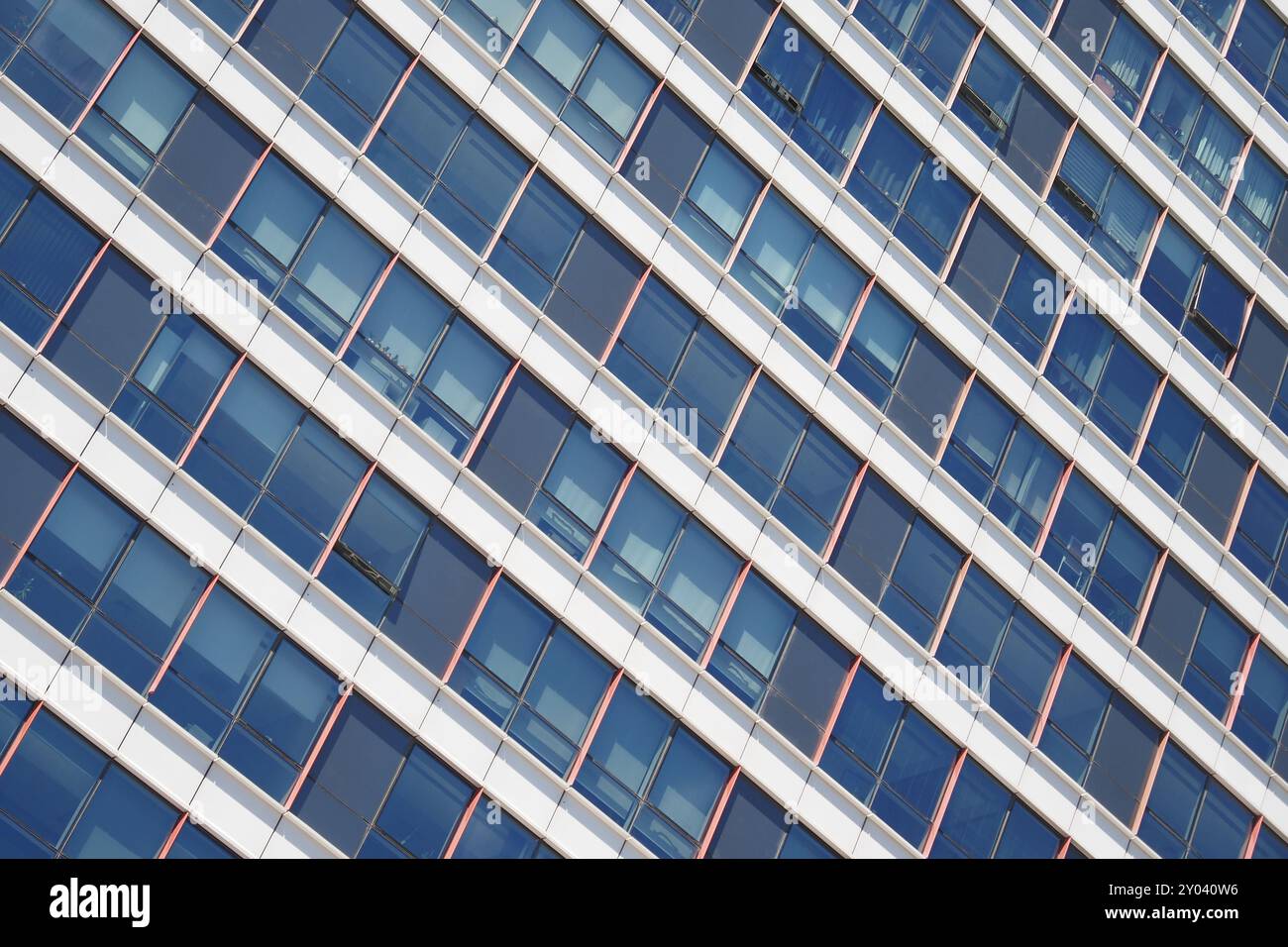 A modern office building facade with slanted glass windows reflecting ...