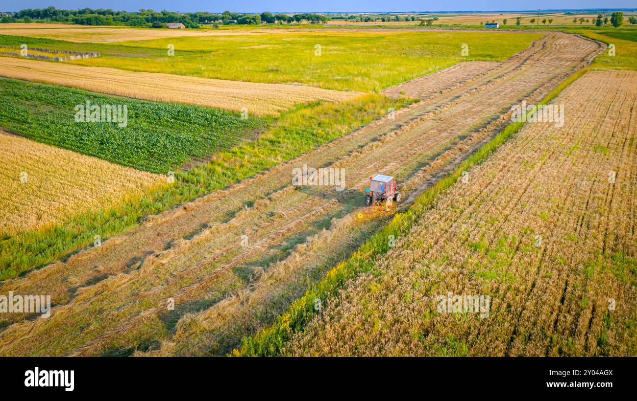 Tractor with attached mechanical rake is turning and gathering dry ...