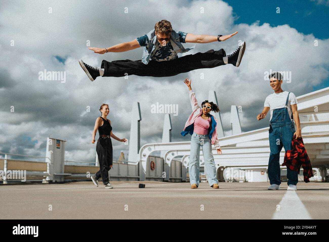 Young man doing split in mid-air while male and female friends standing ...