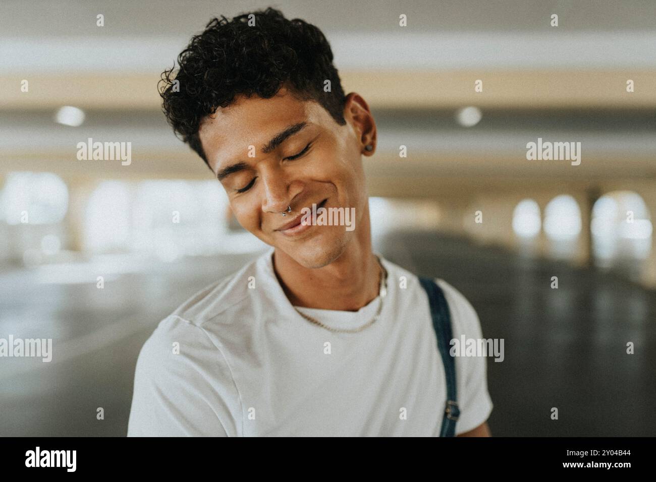 Smiling young man with eyes closed and pierced nose at parking garage ...