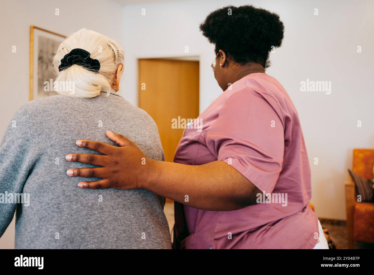 Side view of female caregiver assisting senior woman while walking in ...