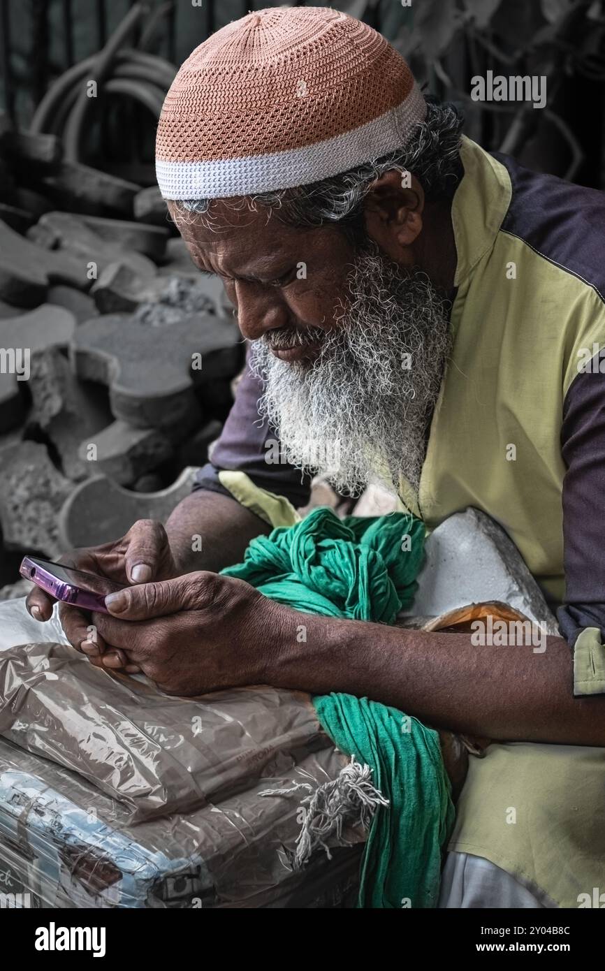 An older muslim man sitting on the street looking at his phone. Old man ...