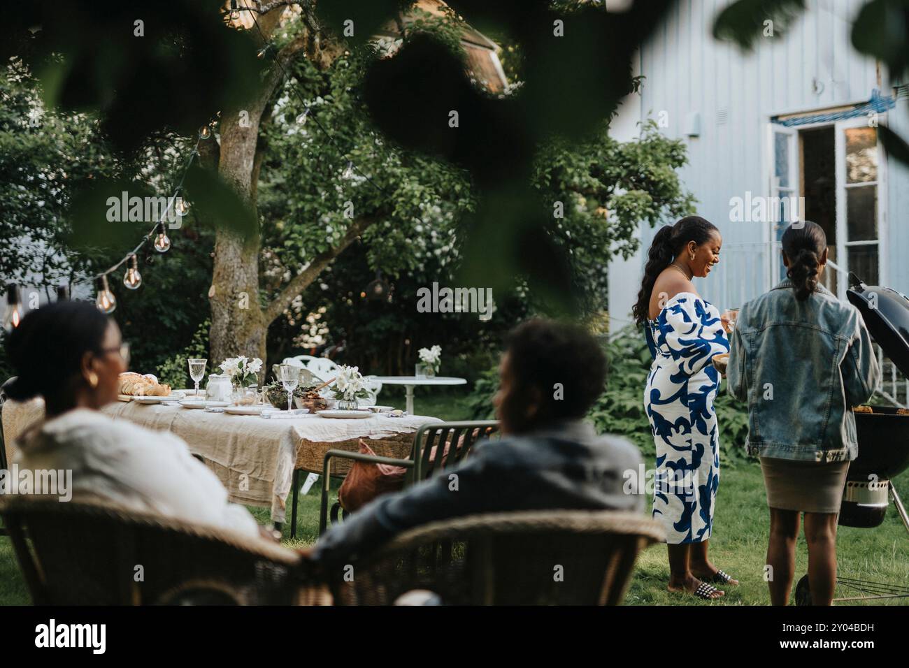 Female family members barbecuing during social gathering at garden ...