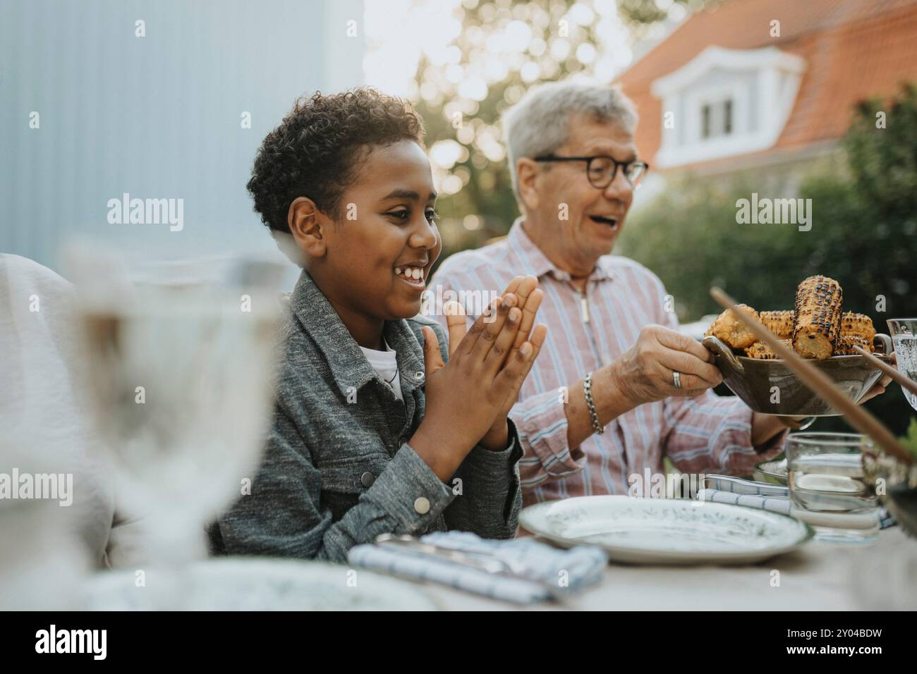 Excited boy clapping while having lunch with grandfather at garden ...