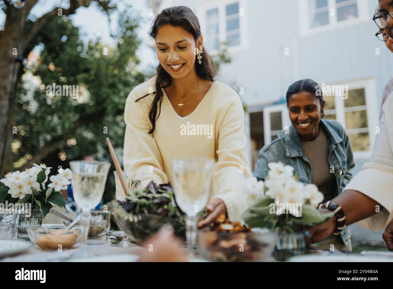 Happy teenage girl setting table for lunch with family members at ...