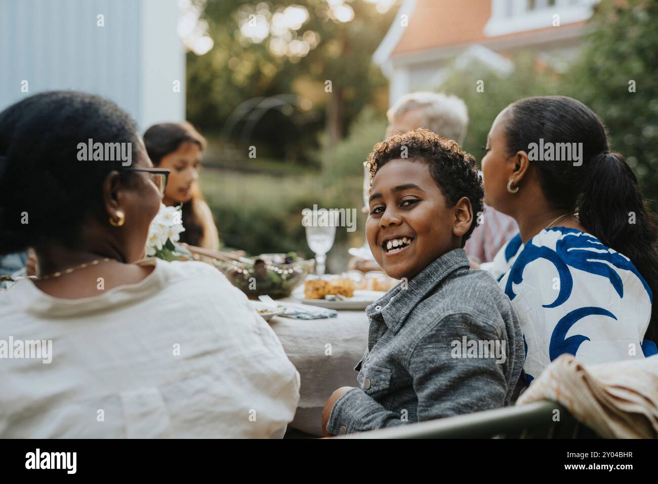 Portrait of playful boy looking over shoulder while sitting with family ...