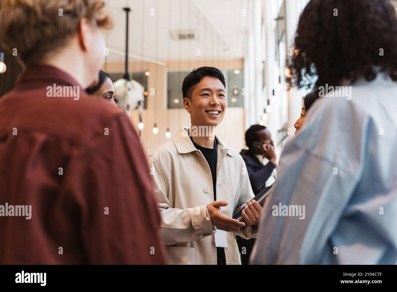 Smiling young male entrepreneur discussing with group of delegates ...