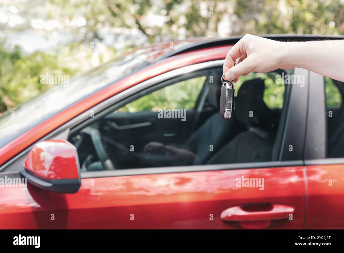 A close-up of a hand holding a car key next to a red vehicle. Concept ...