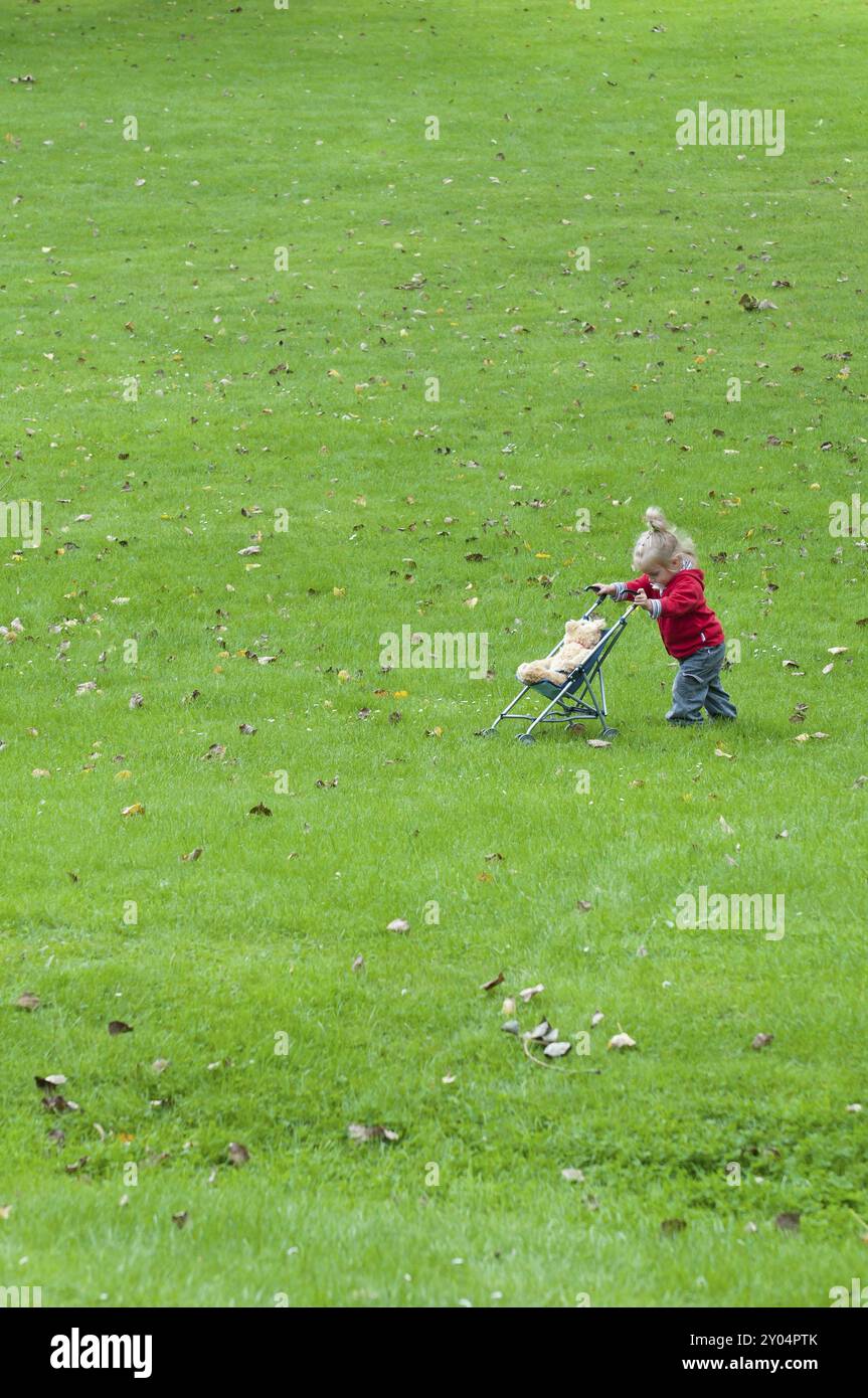 Little girl pushing a doll buggy across a large green meadow, Cute ...