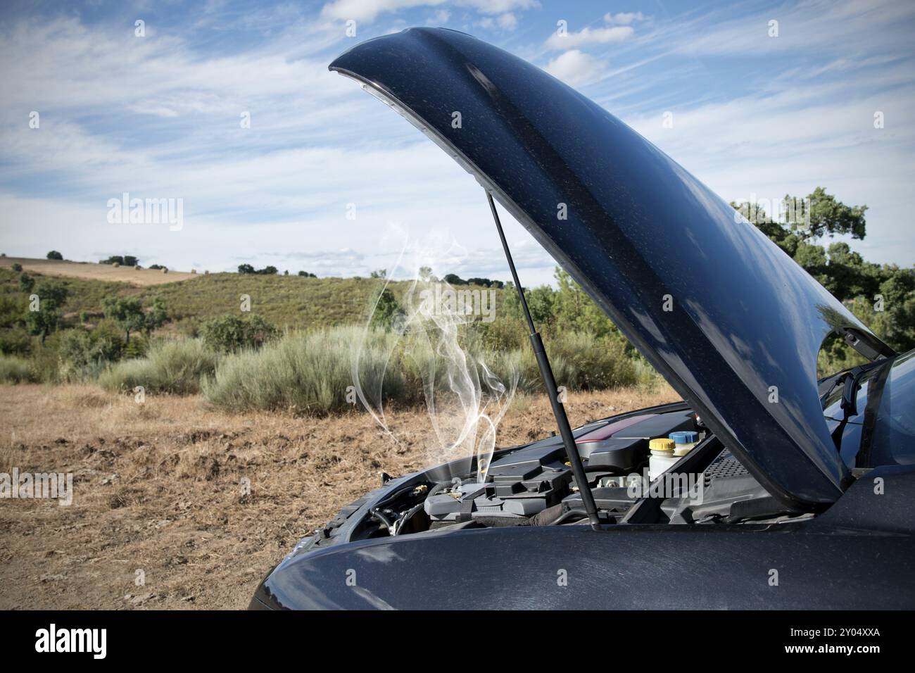 Close up of a broken down car, engine open with smoke, in a rural area ...
