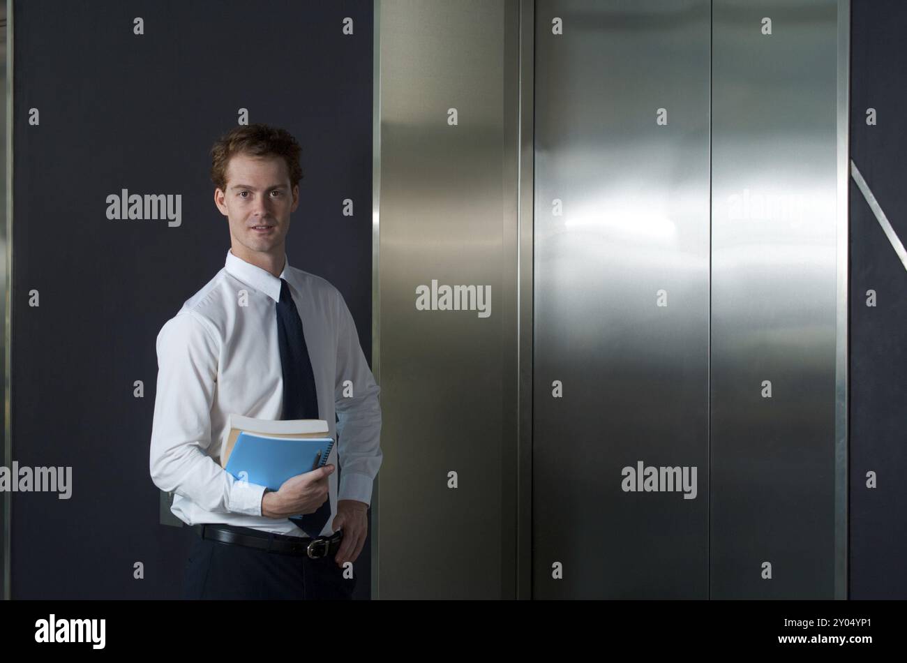 A happy and smiling office worker waiting at the elevator in a typical ...