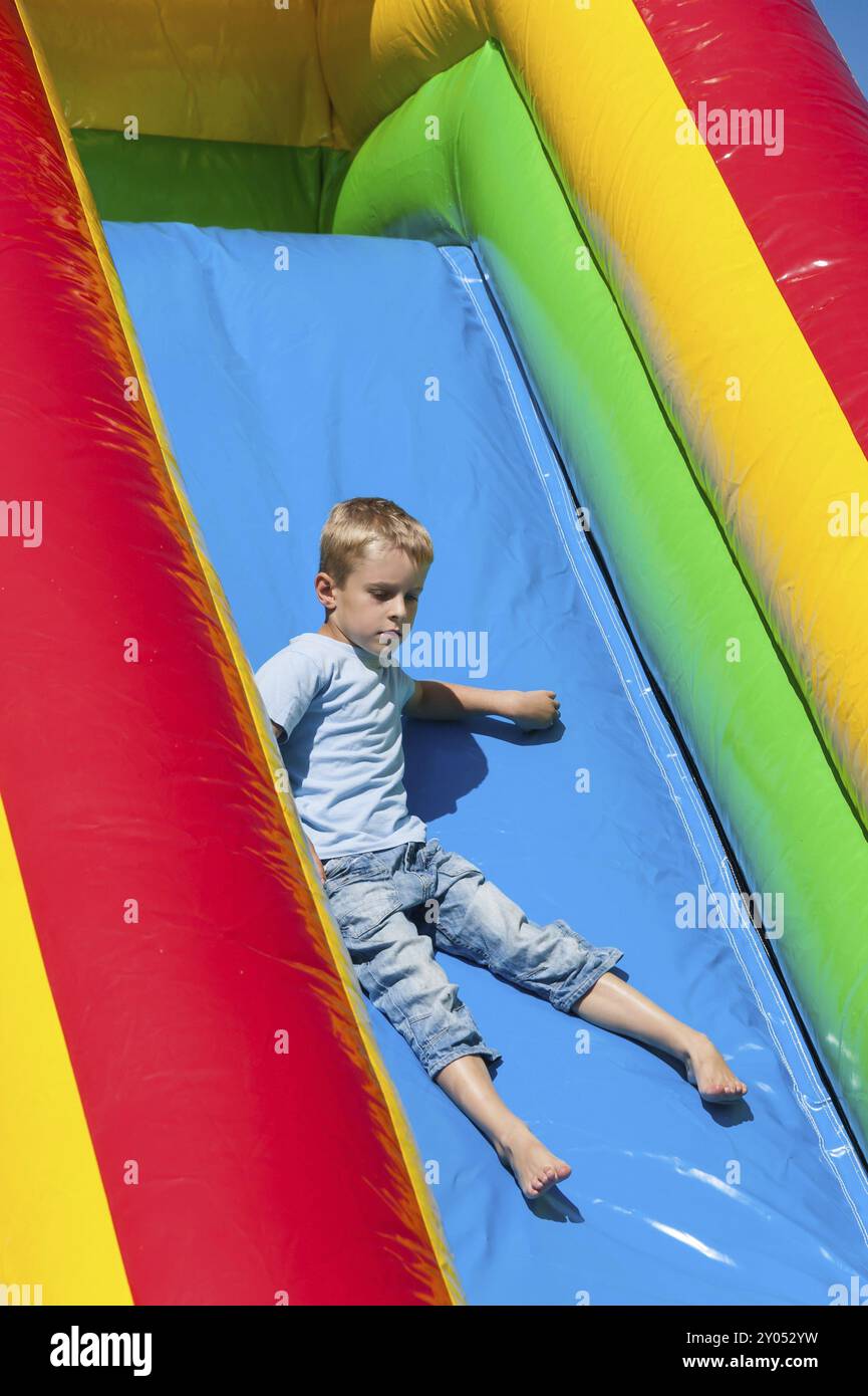 A small barefoot boy slides down a large inflatable slide with great ...