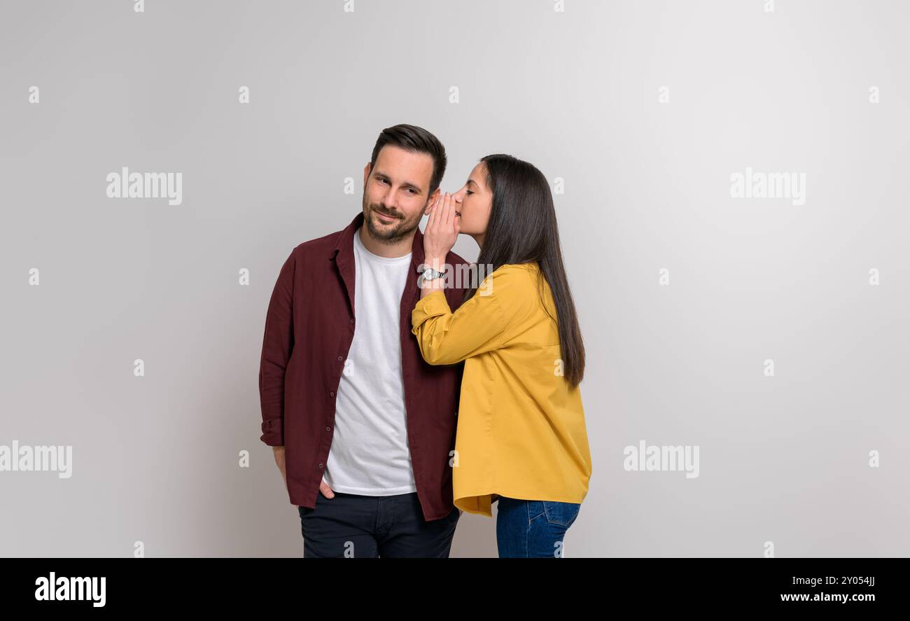 Young girlfriend whispering secret in handsome boyfriend's ear while ...