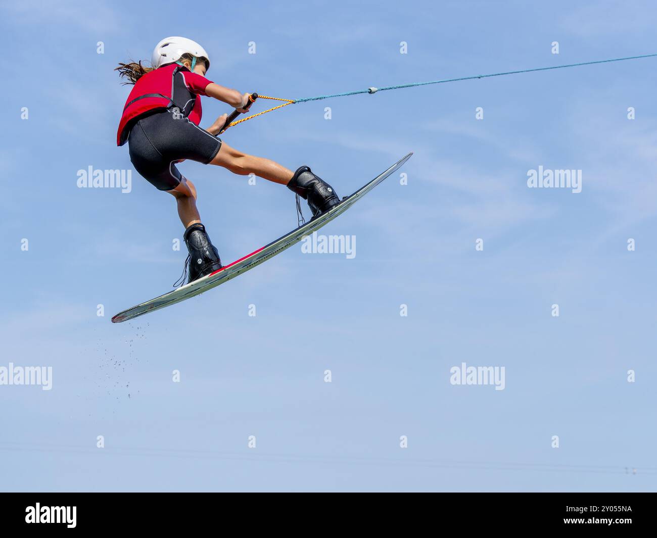 Boy or girl jumping with wakeboard, red life jacket, water sports ...