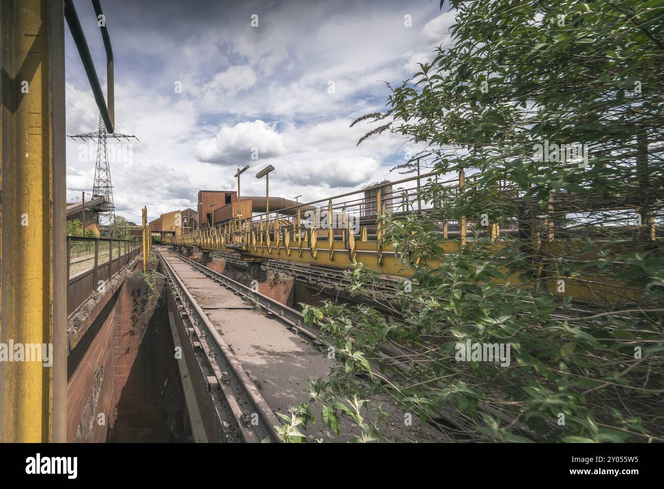 Industrial plant with overgrown rails and rusty metal bridges under a ...