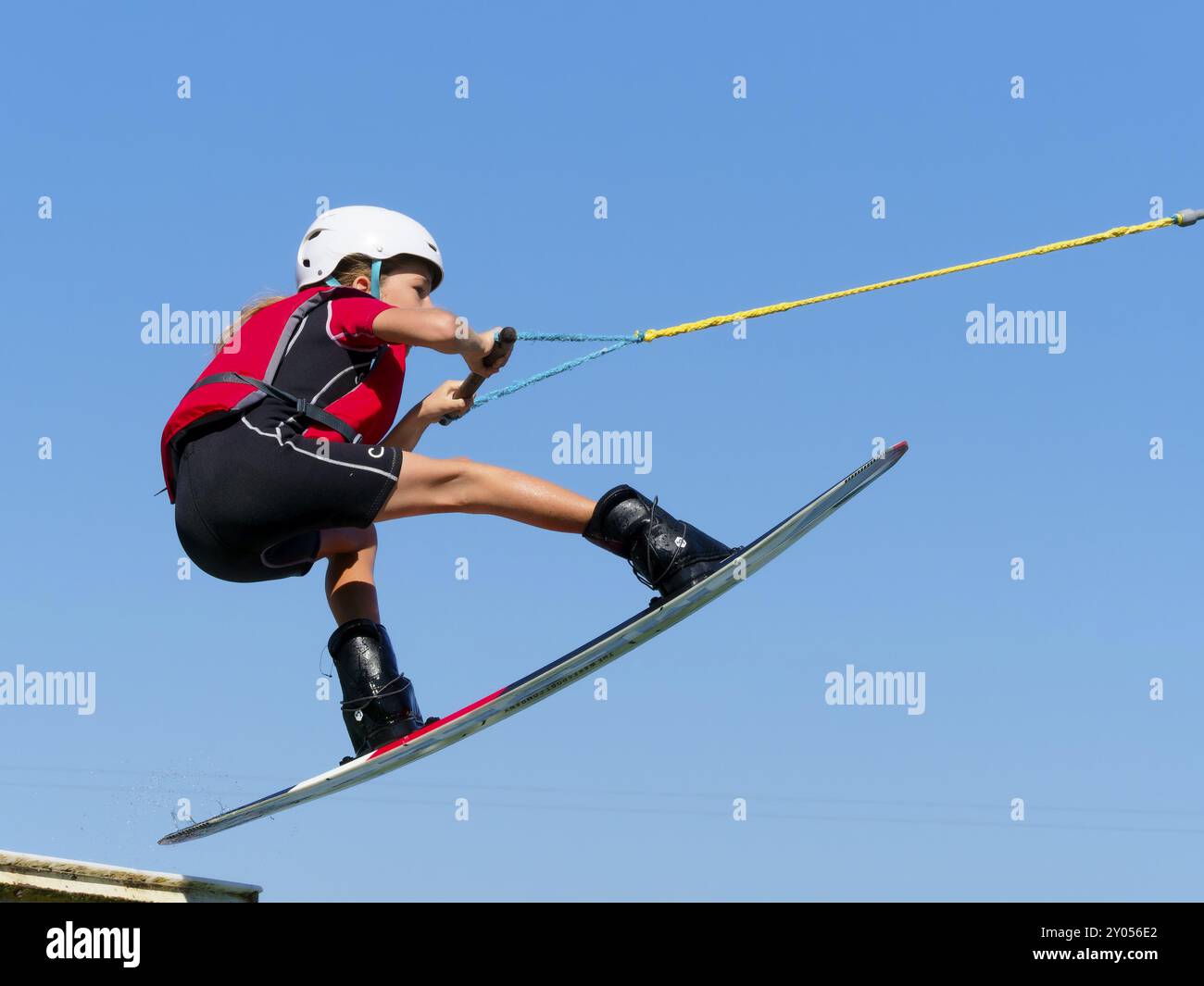 Boy or girl, jump over jump with wakeboard, red life jacket and water ...